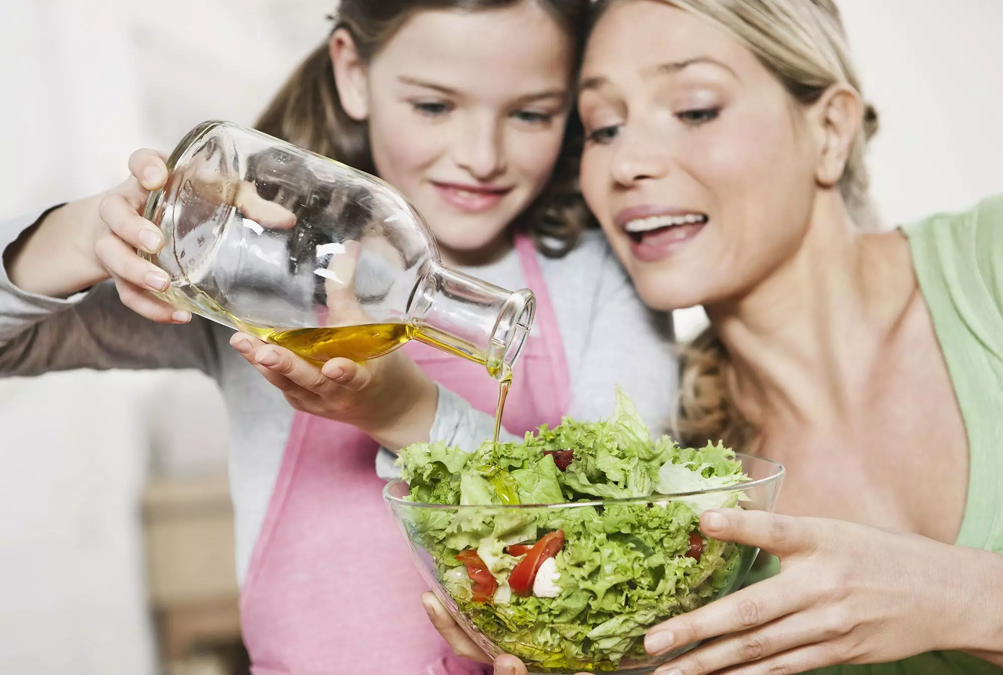 a woman and her daughter dress a salad with olive oil