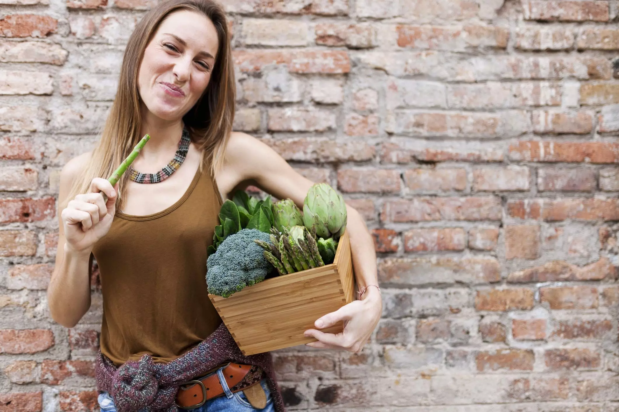 млада девојка се насмевнува со кутија со зеленчук во рацете