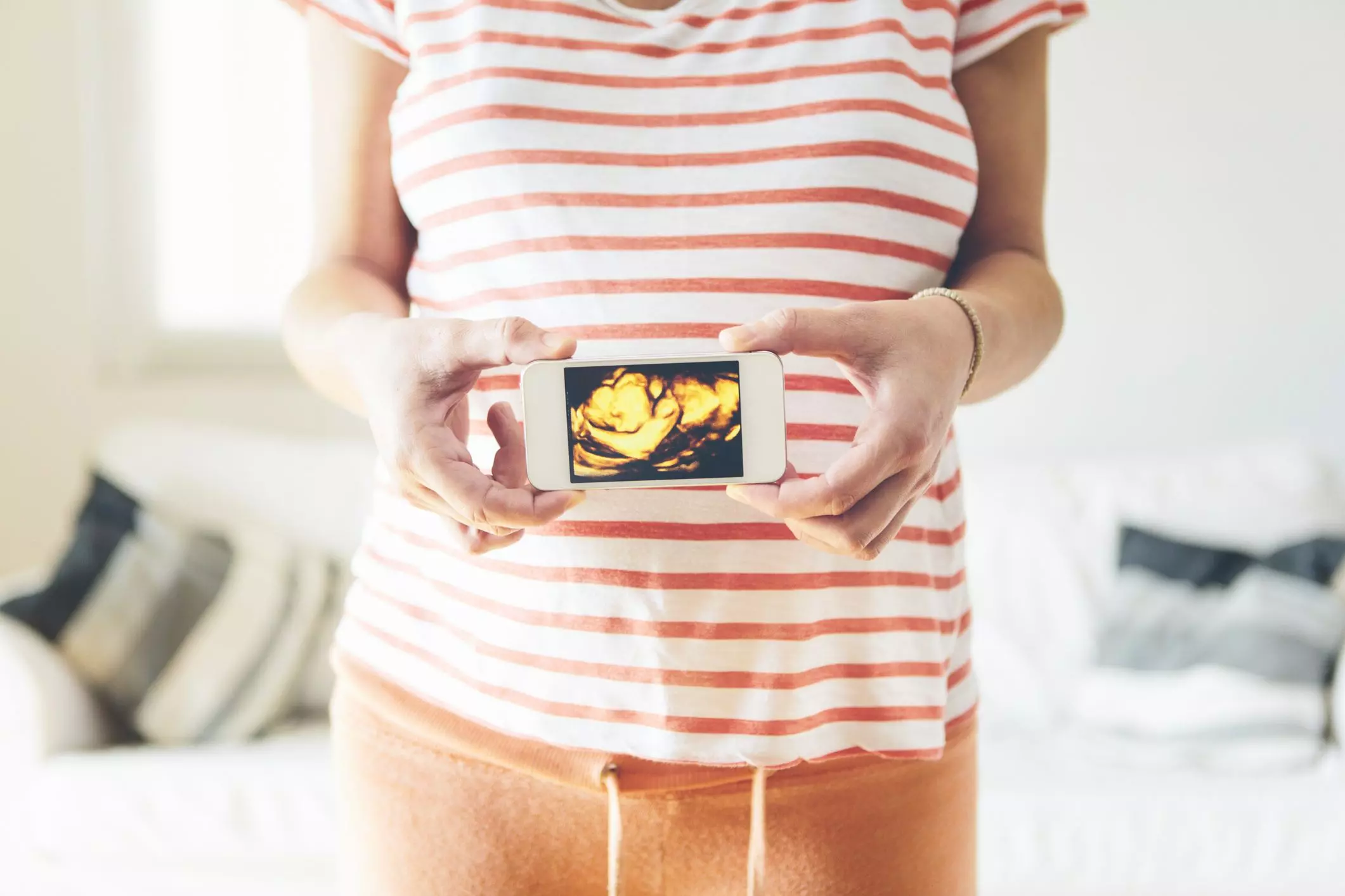 en gravid tjej i randig t-shirt poserar med sin mobil