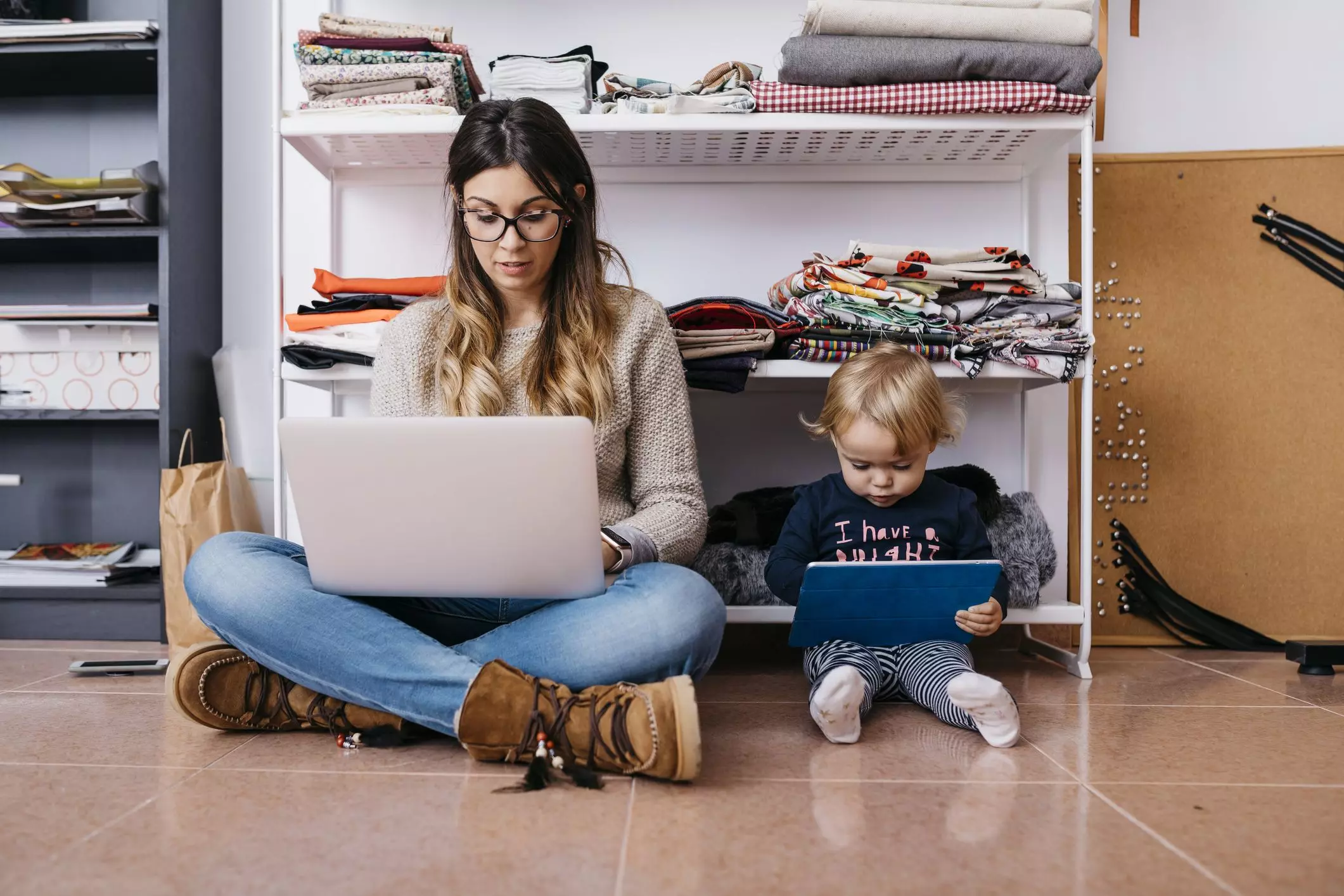 母親和小女兒坐在家裡的地板上，使用筆記本電腦和平板電腦