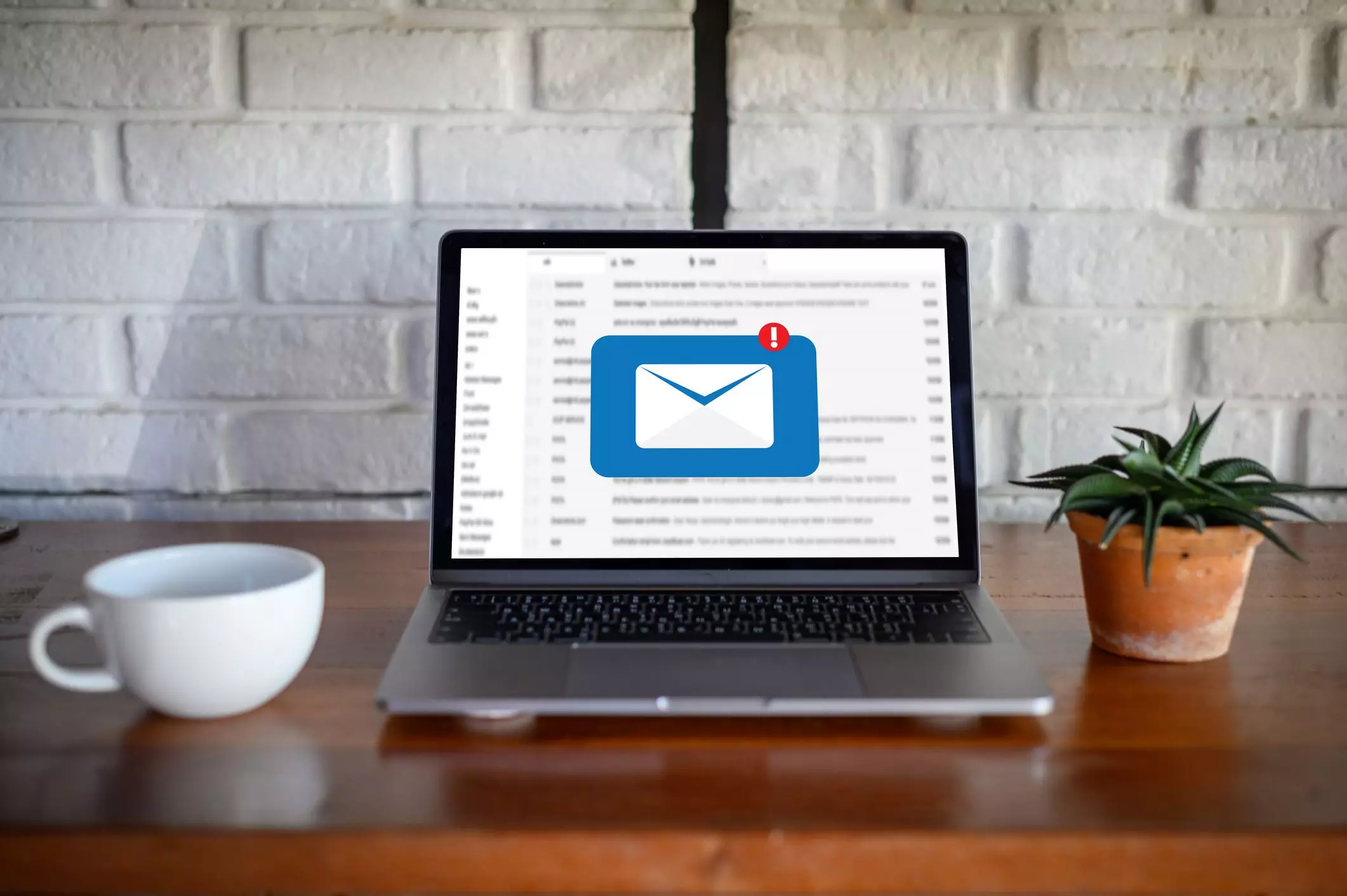 pantalla do portátil con caixa de entrada de correo electrónico aberta na mesa xunto a cunca e cacto
