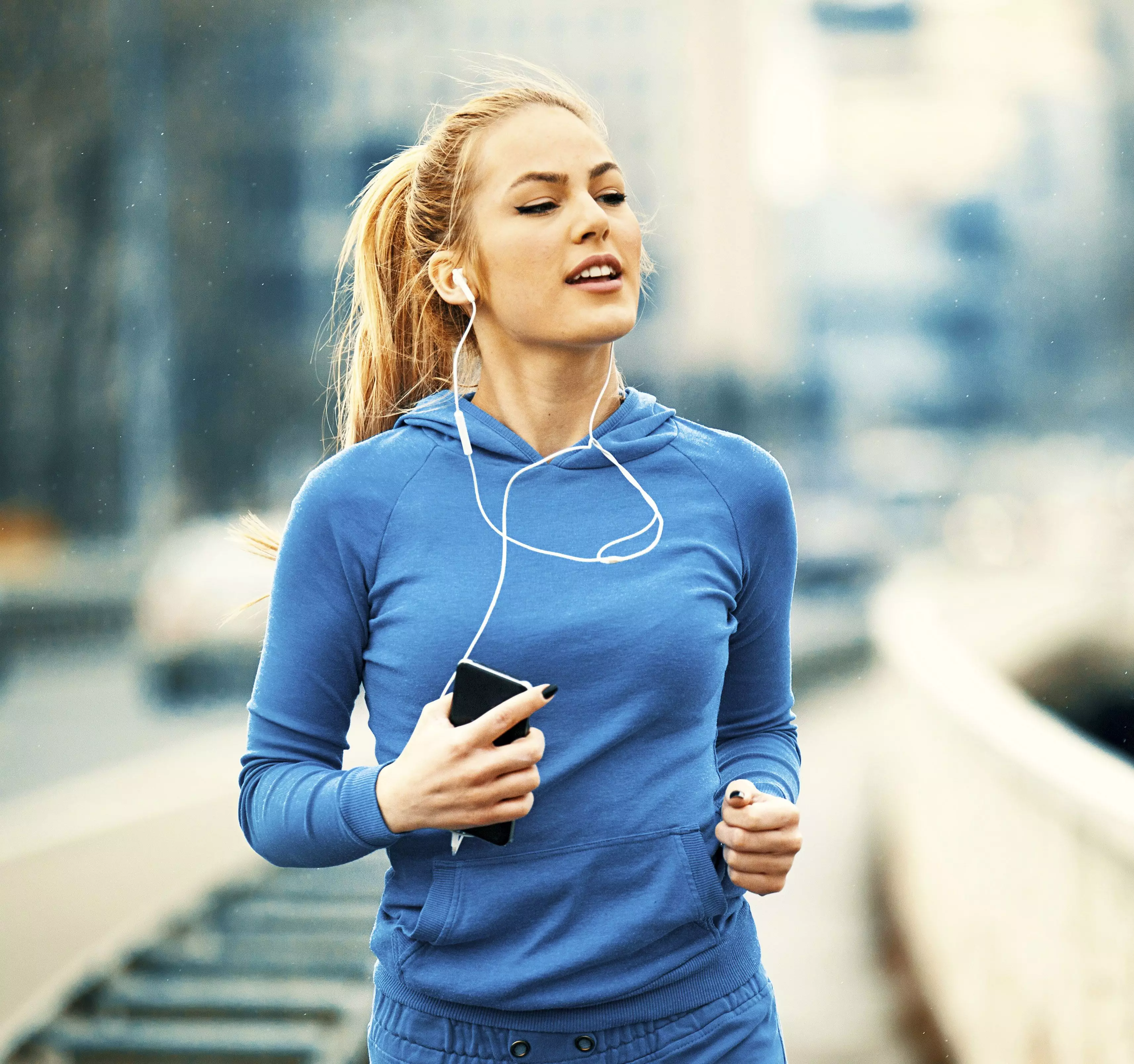 Glad ung kvinne som lytter til musikk mens hun jogger på broen