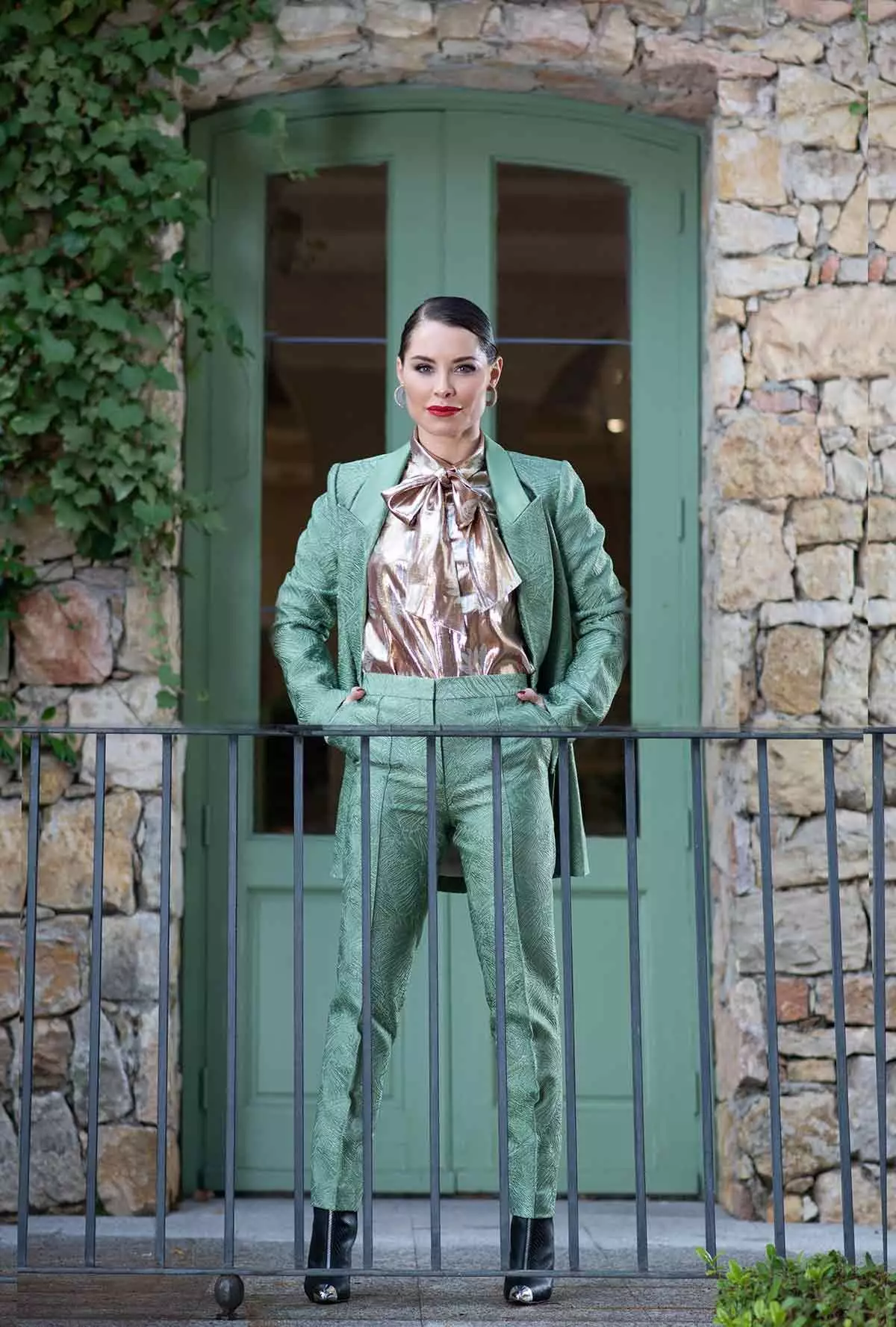 Співачка носить зелений костюм від By Malene Birger By Zalando; золота сорочка з бантом від Cézane; ботильйони з металевим носком від Exé Shoes; і сережки Patricia Nicolas.