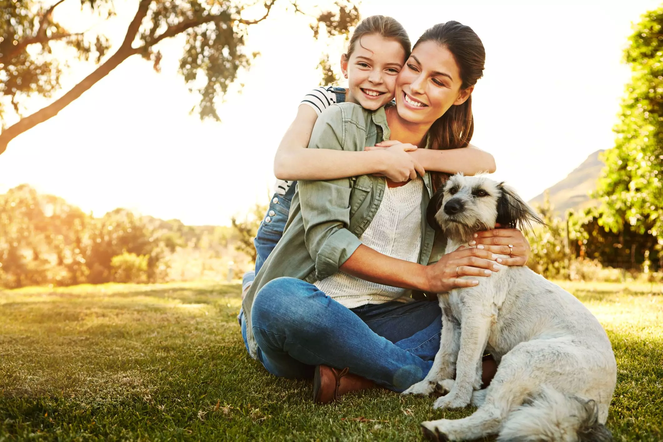 a girl hugs her mother in a park where they are with their pet