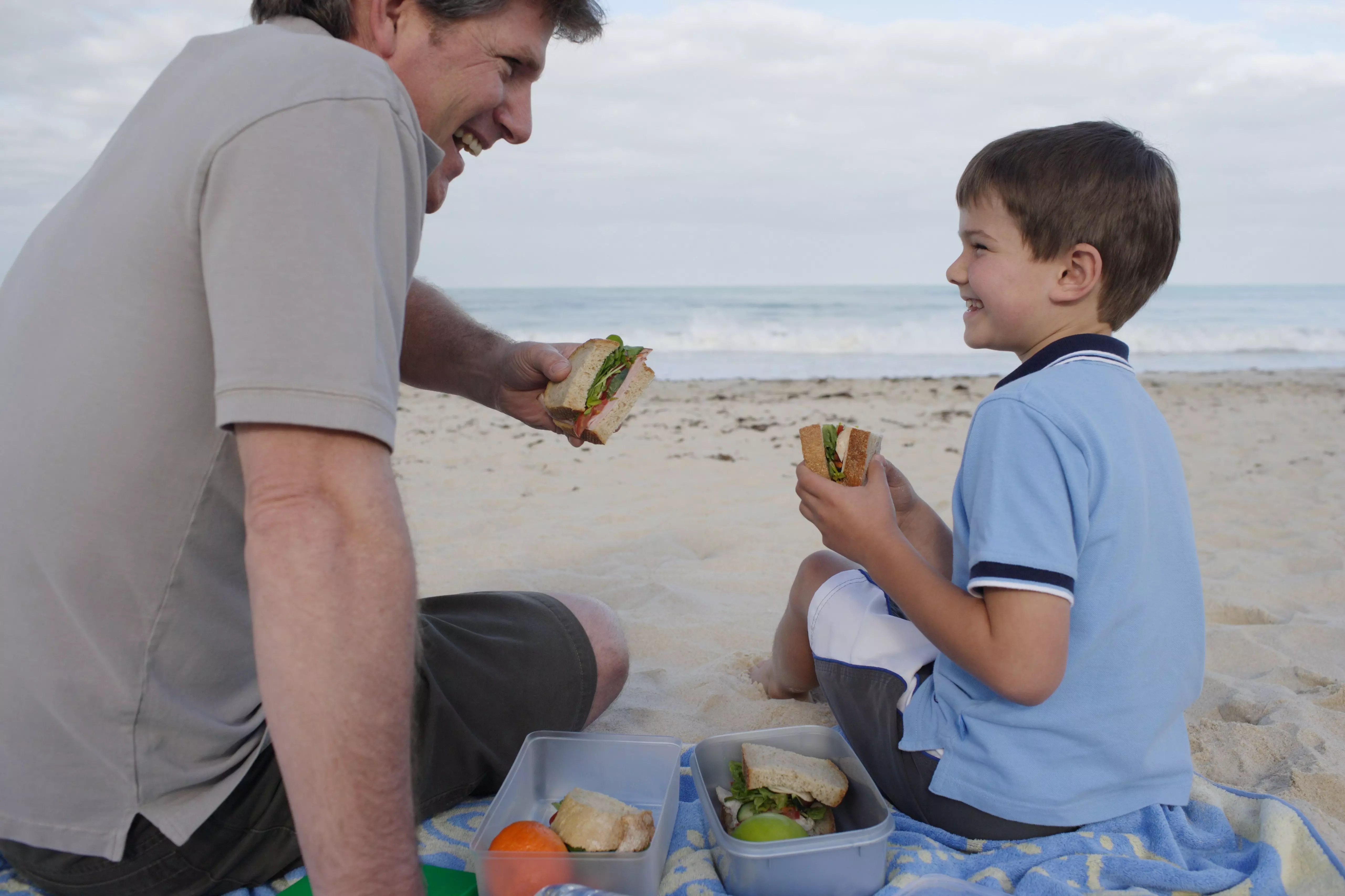 een vader en zijn zoon eten een broodje op het strand