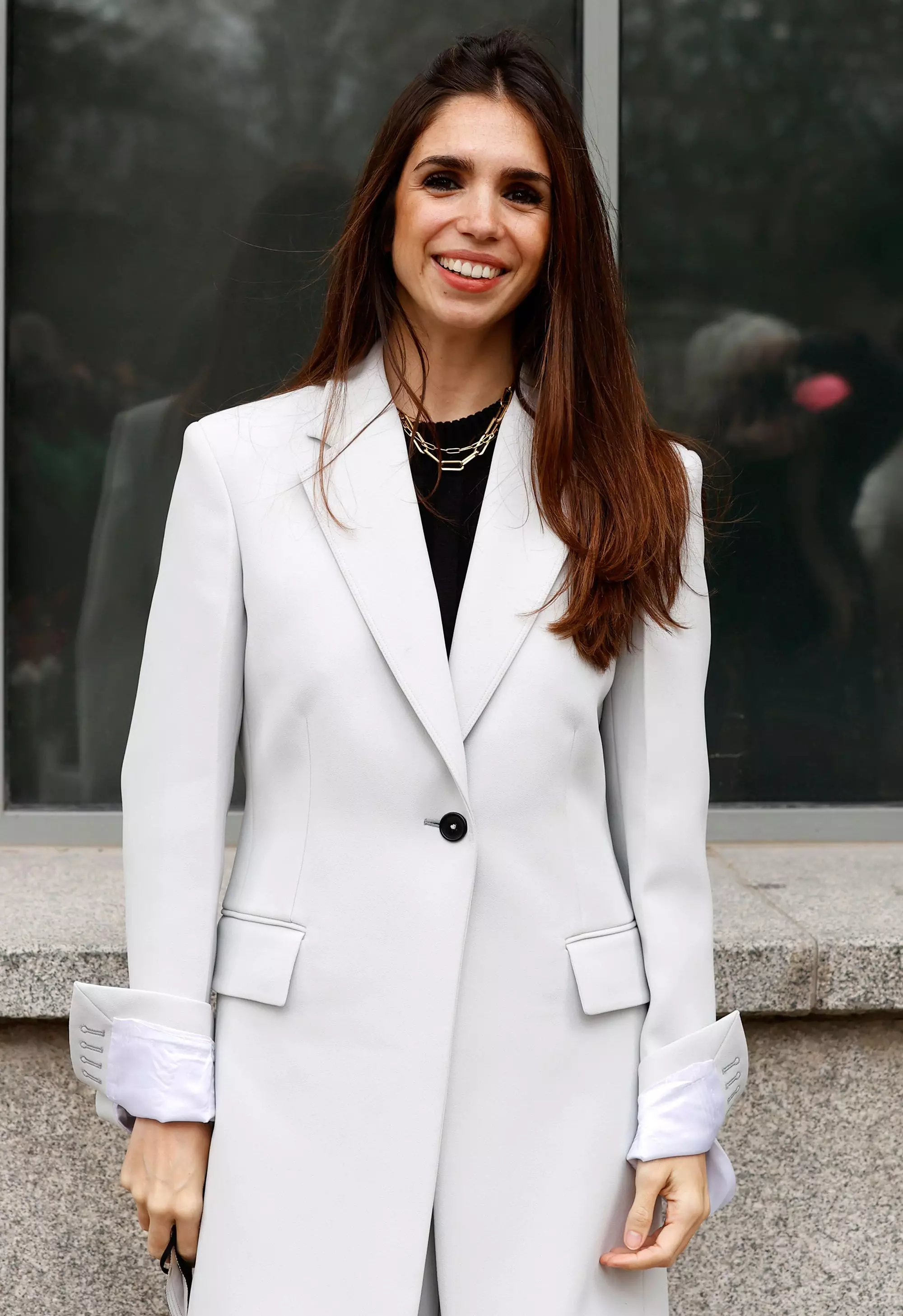 Lolita's daughter, in a medium shot, smiles in an oversize gray blazer and black T-shirt