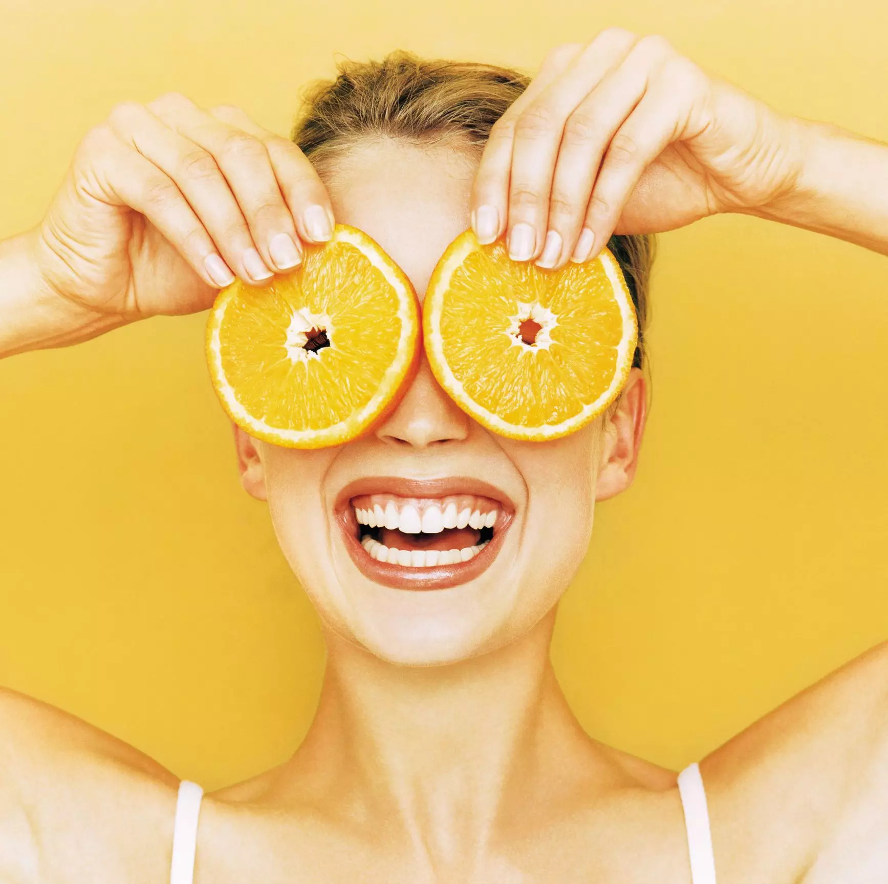 young woman holding orange slices in front of eyes, close up, portrait