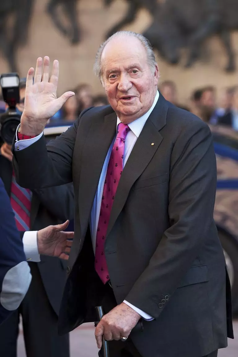 king juan carlos waving with his hand raised in the street